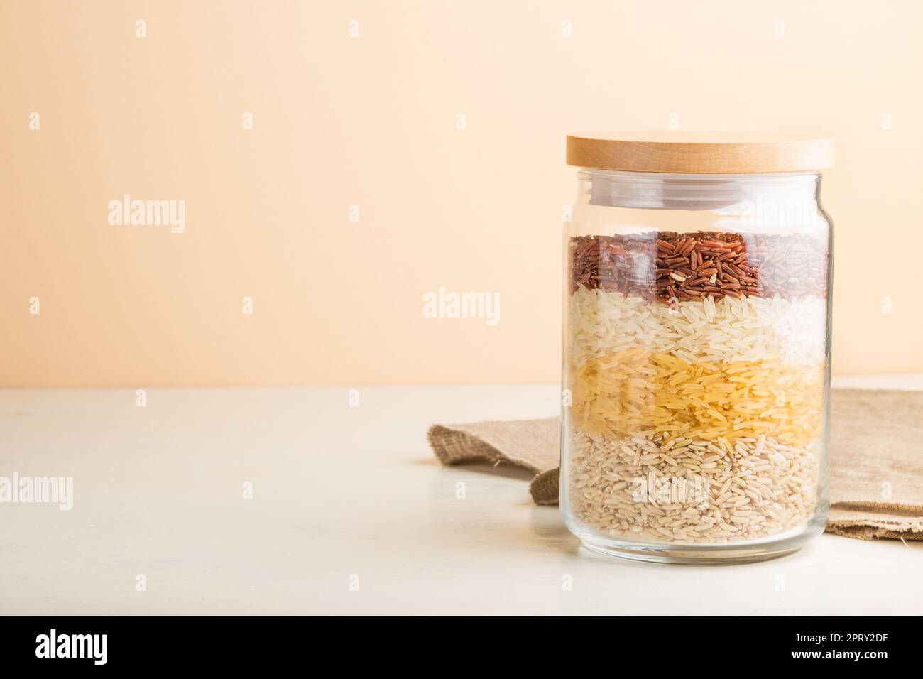 glass jar with different kinds of rice poured in layers on white and ...