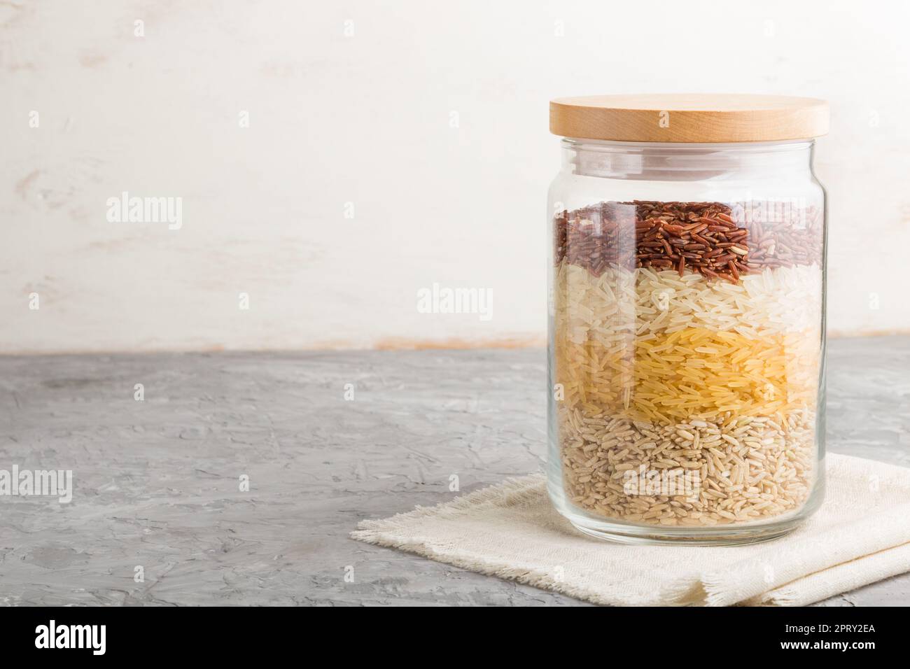 glass jar with different kinds of rice poured in layers on a gray and ...