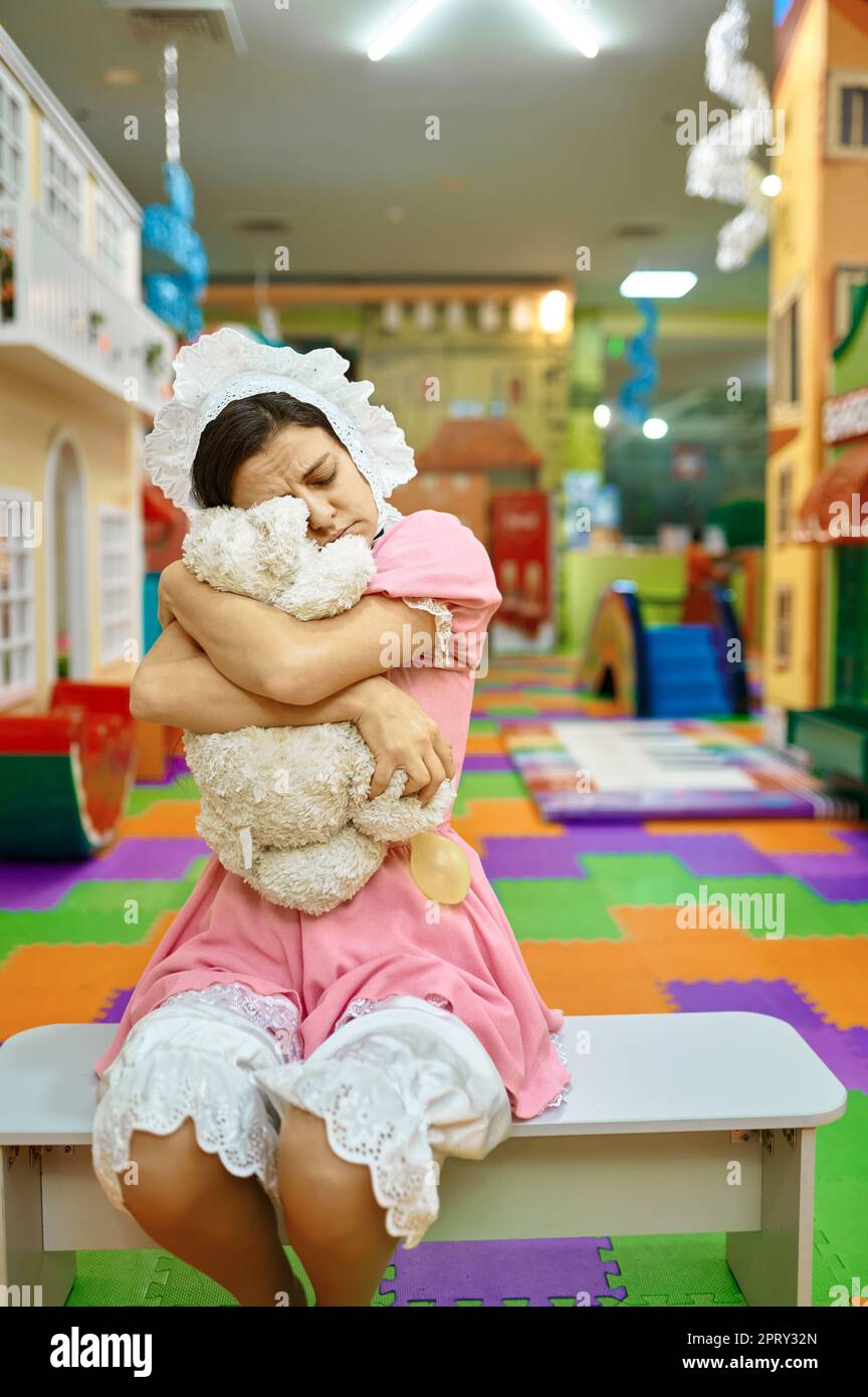 Sad woman wearing like newborn baby hugging teddy bear sitting over ...