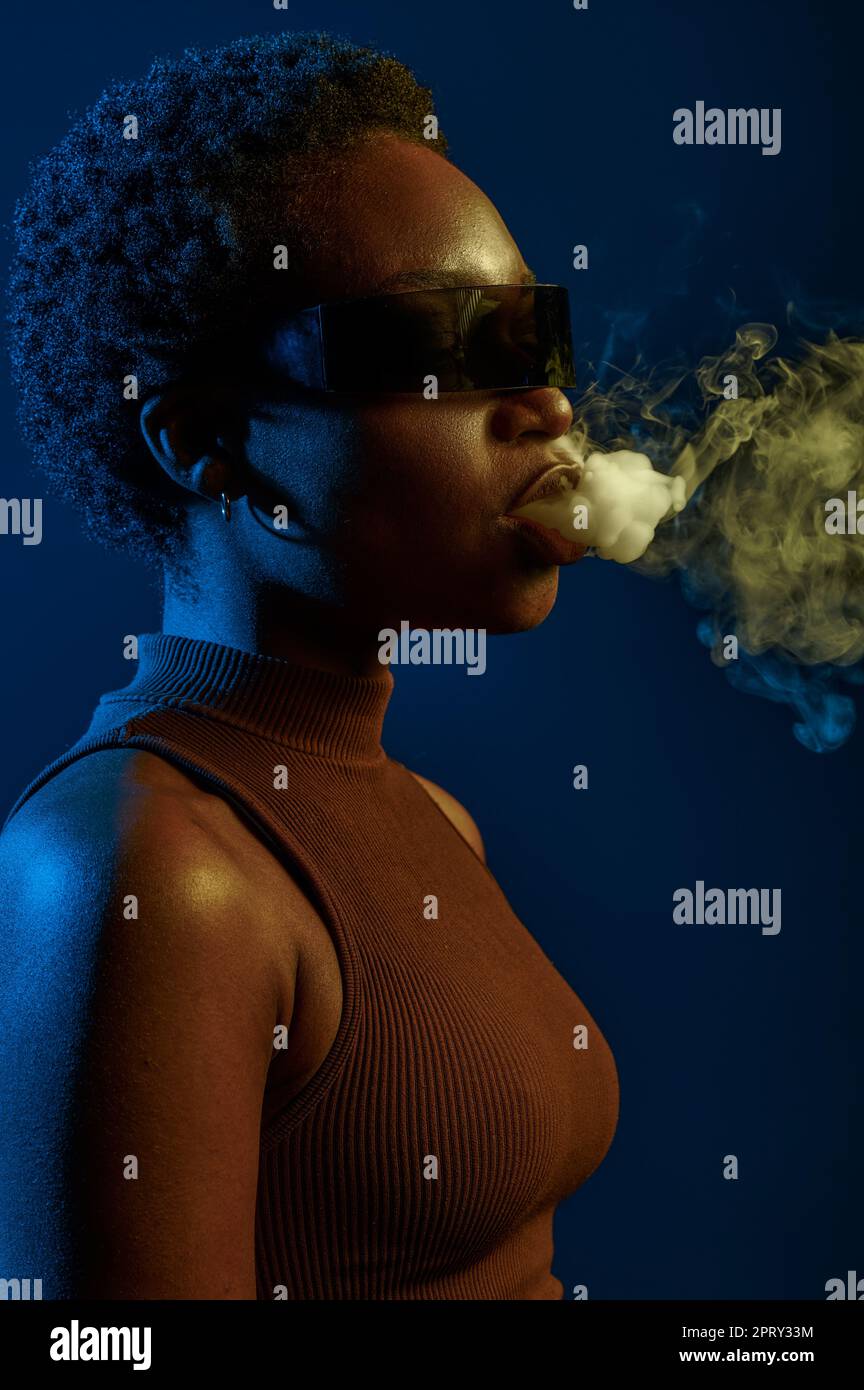 Passion woman blowing smoke curls from mouth over dark studio ...