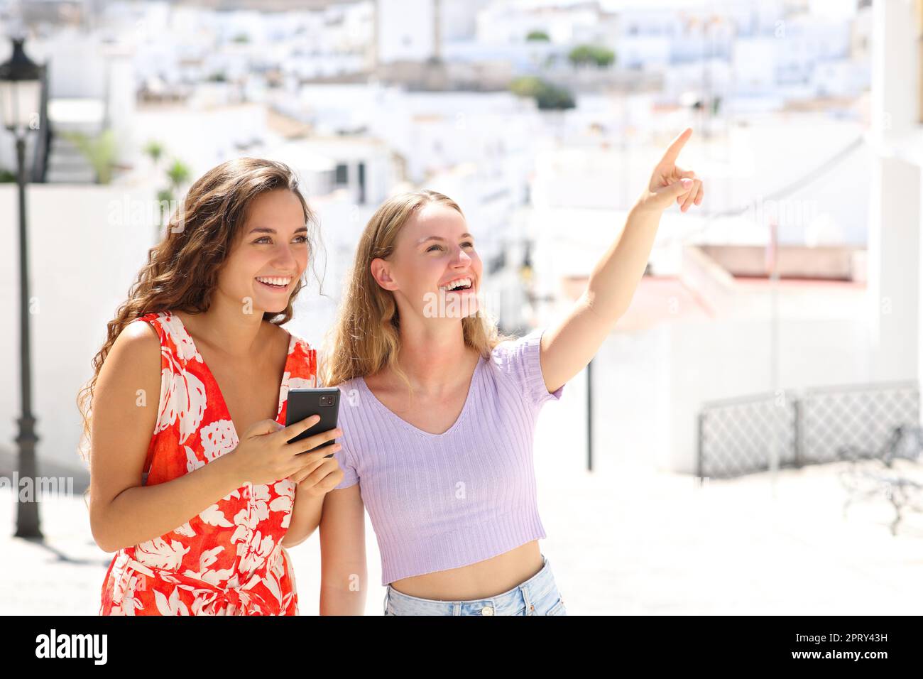 Two happy tourists checking smart phone pointing landmark standing in a ...