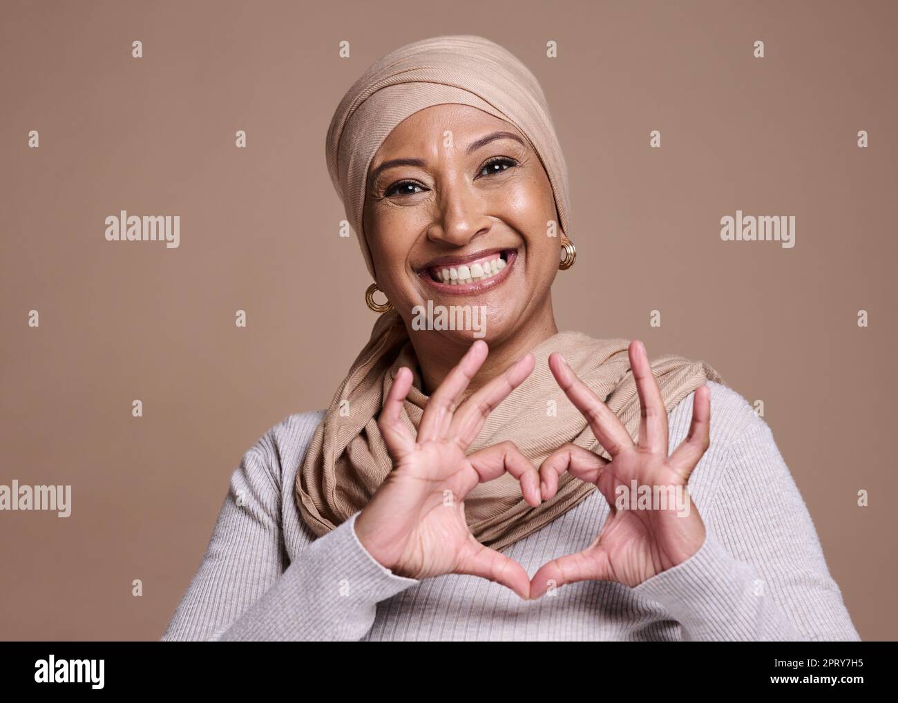 Islam woman, heart and sign with smile, happy and peace against brown ...