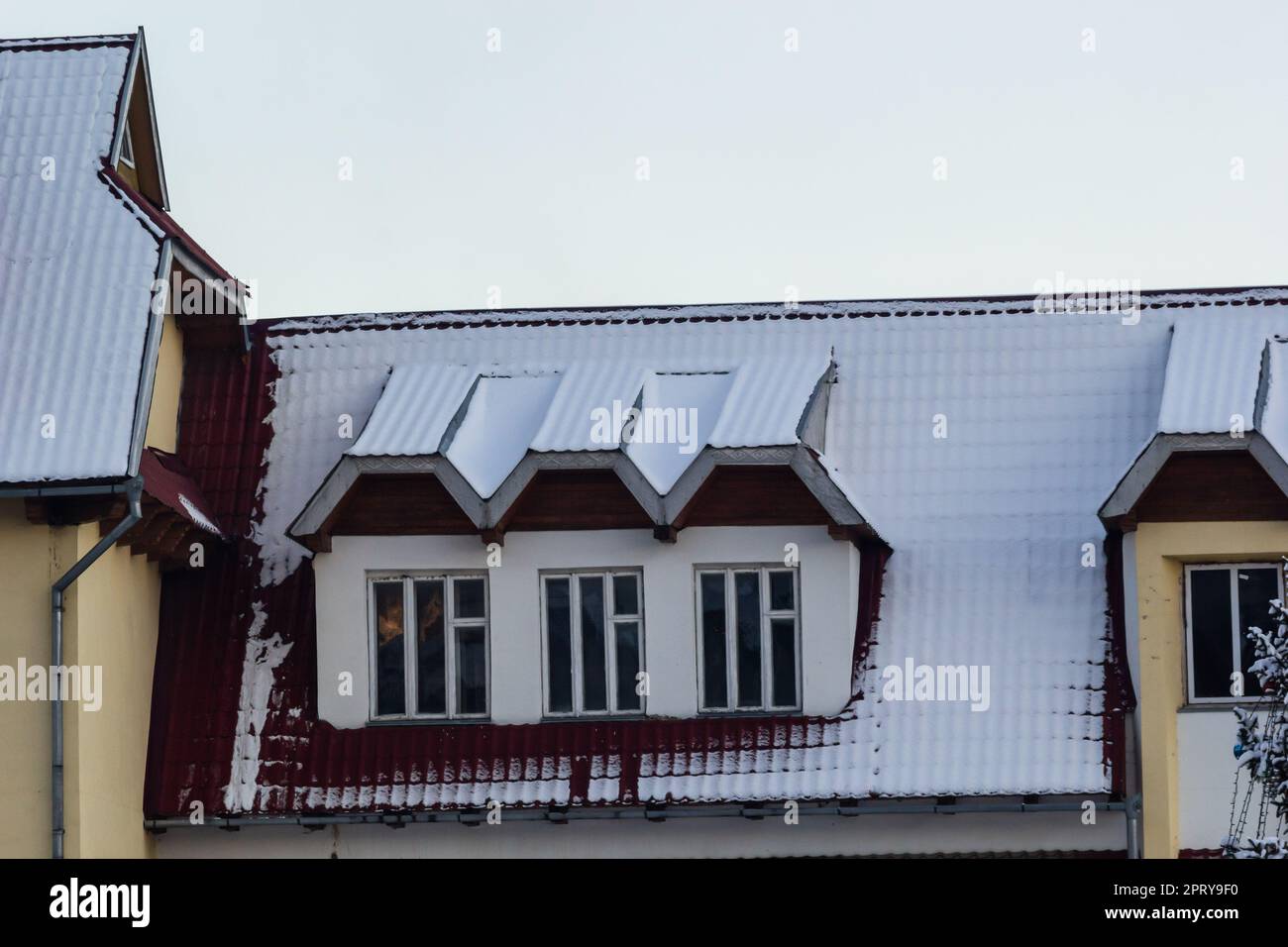 Snow on the roof of a red, brown metal roof of a European house with a ...