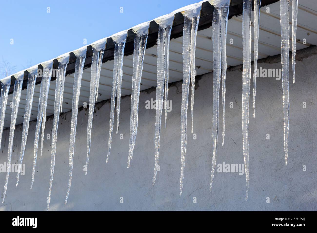 Sharp icicles and melted snow hanging from eaves of roof. Beautiful ...