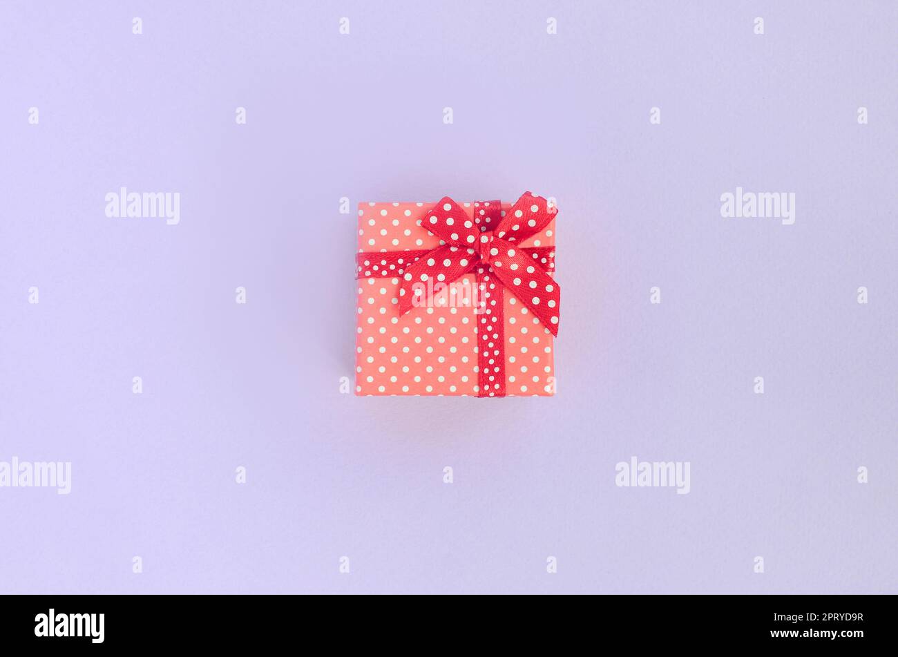 Small red gift box with ribbon lies on a violet background. Minimalism ...