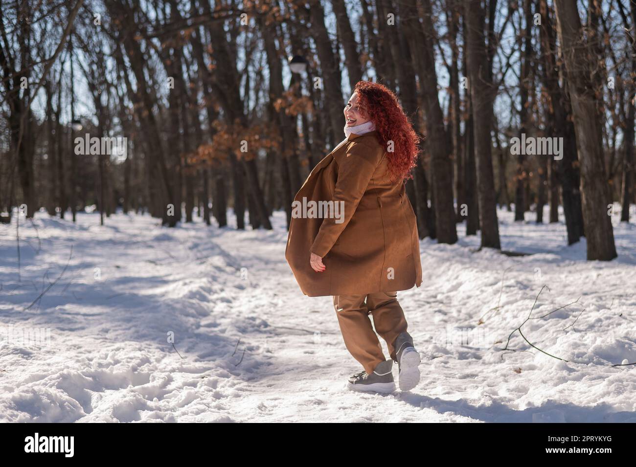 Portrait of an excited red-haired curly fat woman in the park in winter ...