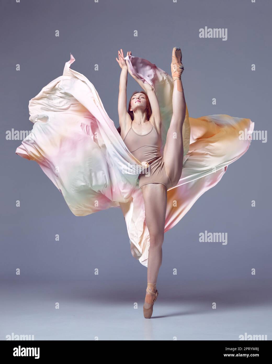 One grace ballerina wearing rainbow dress emotional dancing with fabric over grey studio ...