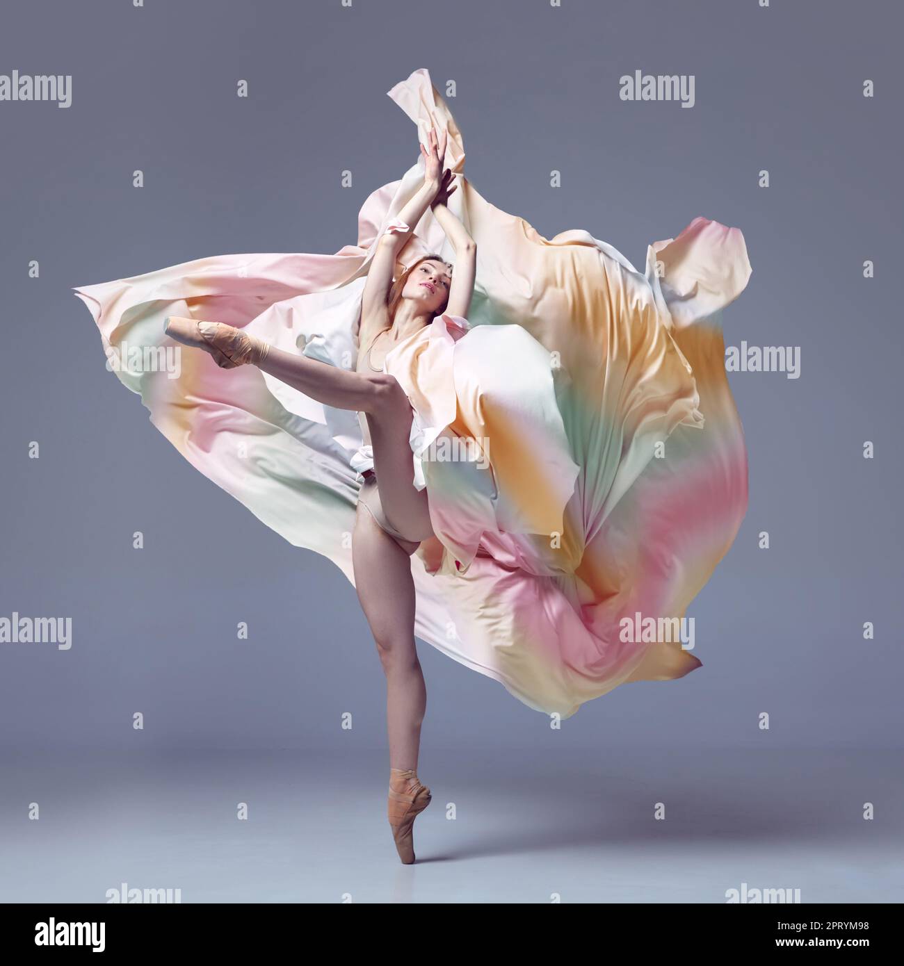 One adorable ballerina wearing rainbow dress emotional dancing with fabric over grey studio ...