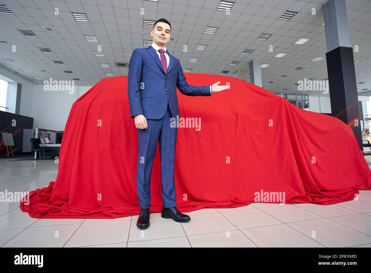Man in a business suit stands in front of a car covered with a red ...