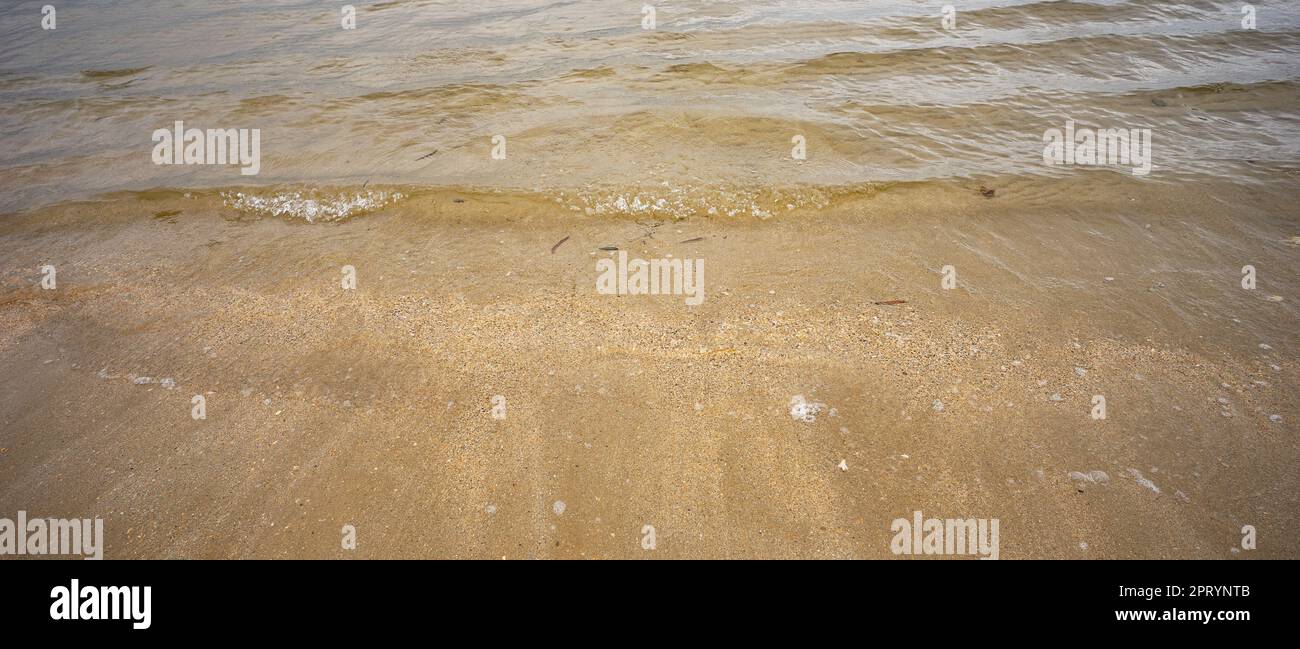 Clear sea water and small waves and ripples crossing a sandy beach and ...