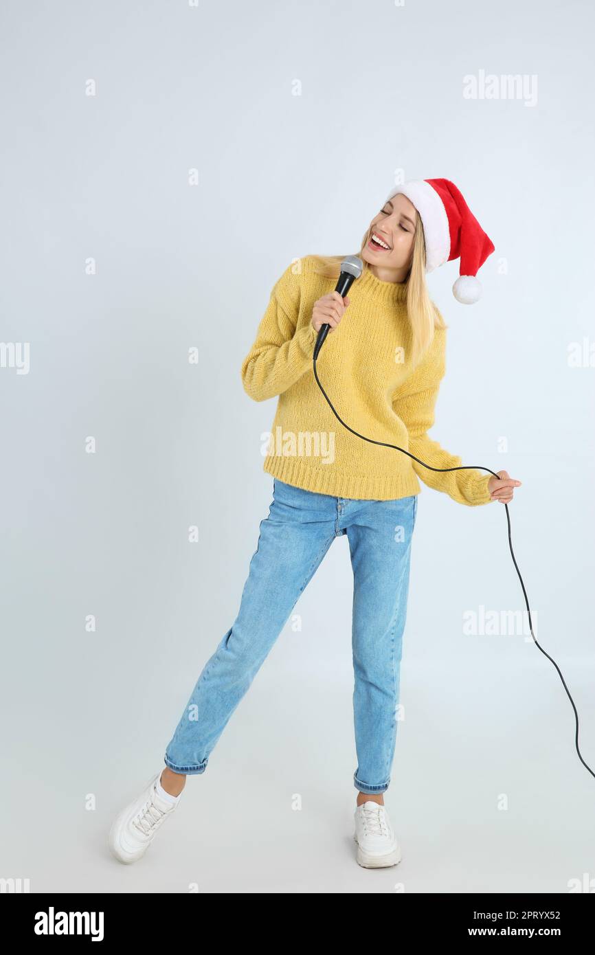 Emotional woman in Santa Claus hat singing with microphone on light ...