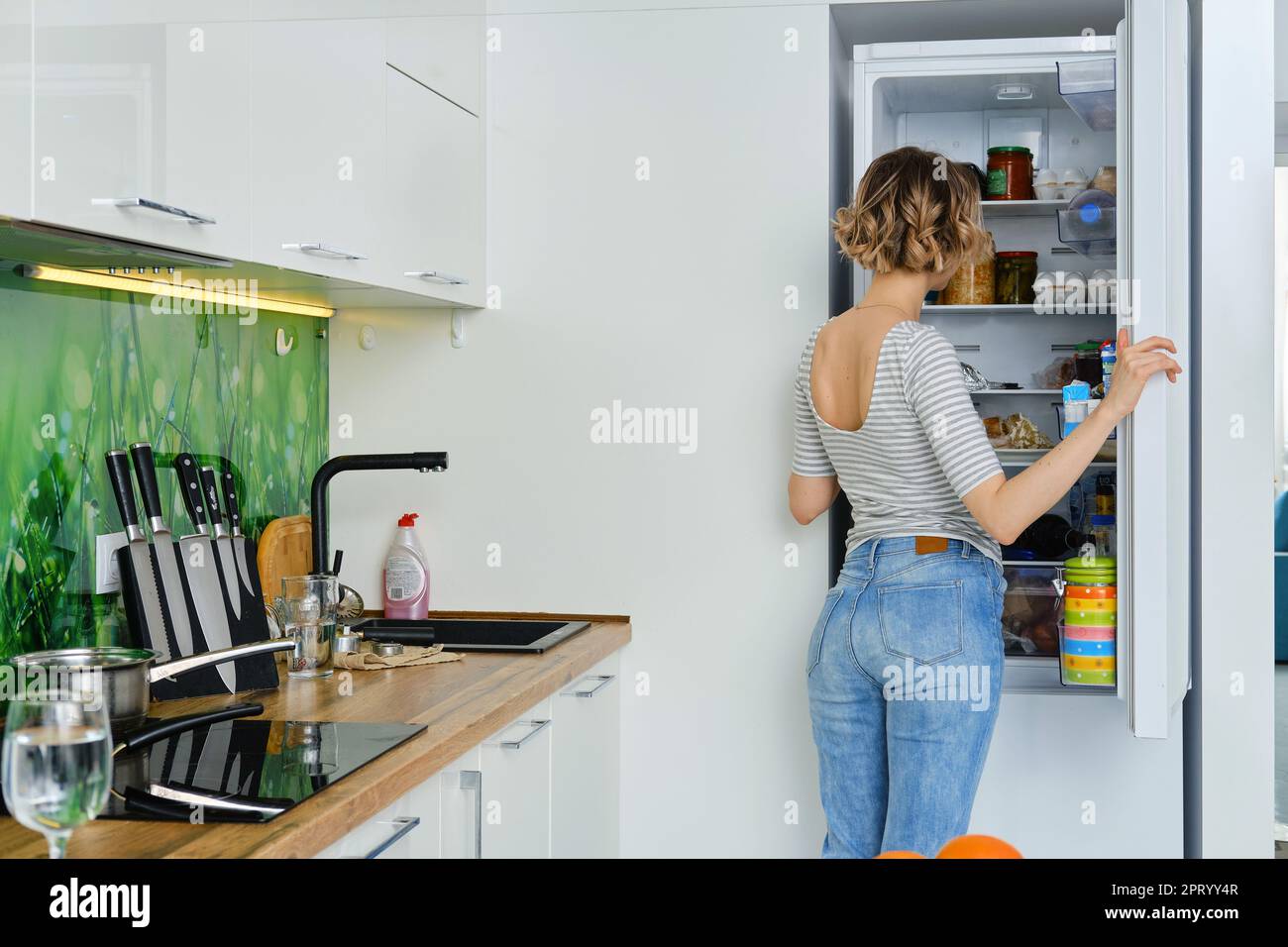Back view of cheerful young woman takes out the fridge breakfast ...