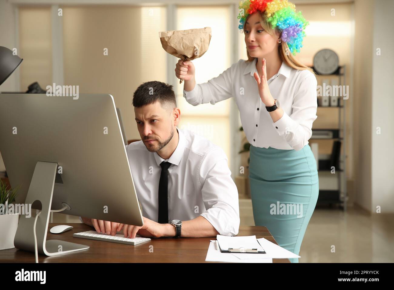 Young woman popping paper bag behind her colleague in office. Funny ...