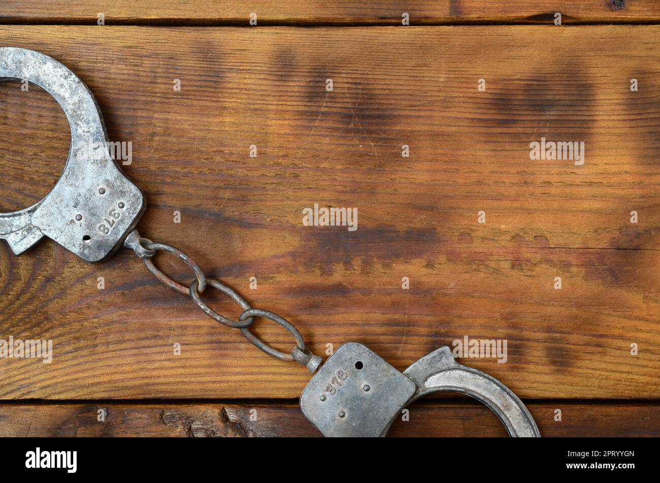 Old and rusty police handcuffs lie on a scratched wooden surface. The ...