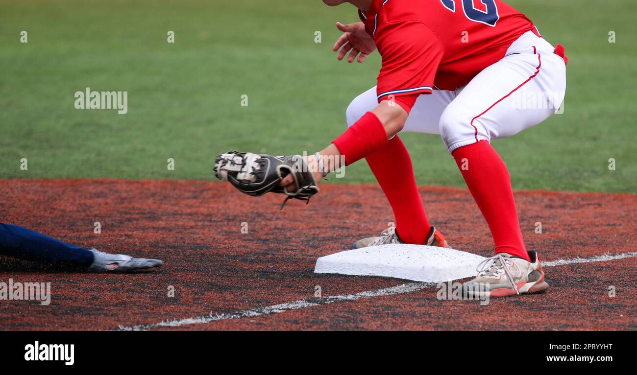 Third baseman ready to tag out the arm of a sliding runner during a ...