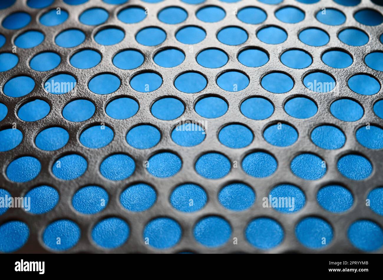 Black metal computer case panel mesh with holes on blue background ...
