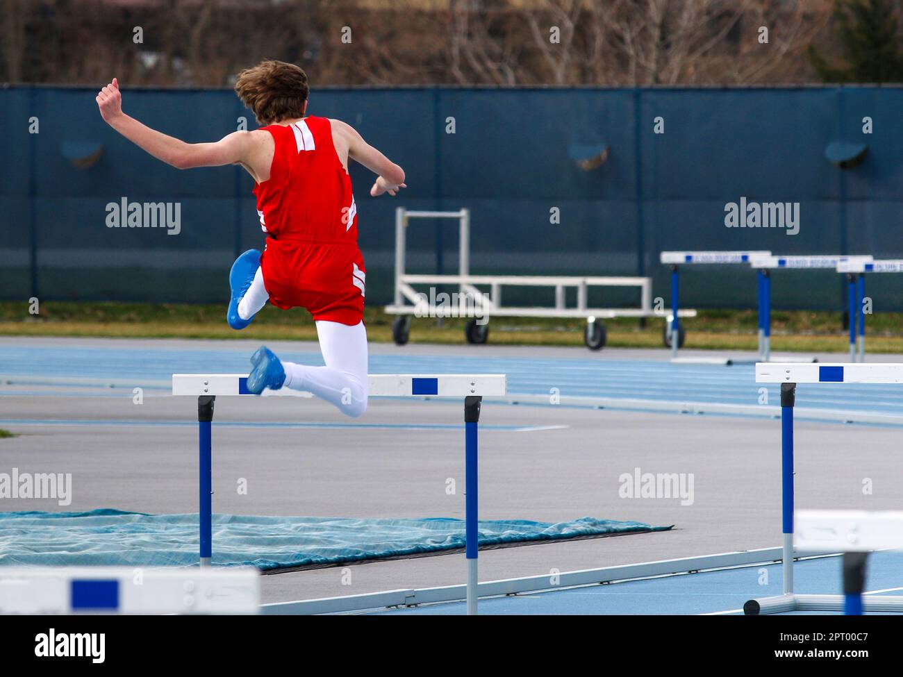 Rear view of a high school boy is running over hurdles on a track ...