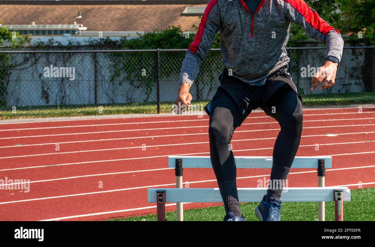 A high school boy is jumping over a track hurdle during track and field ...