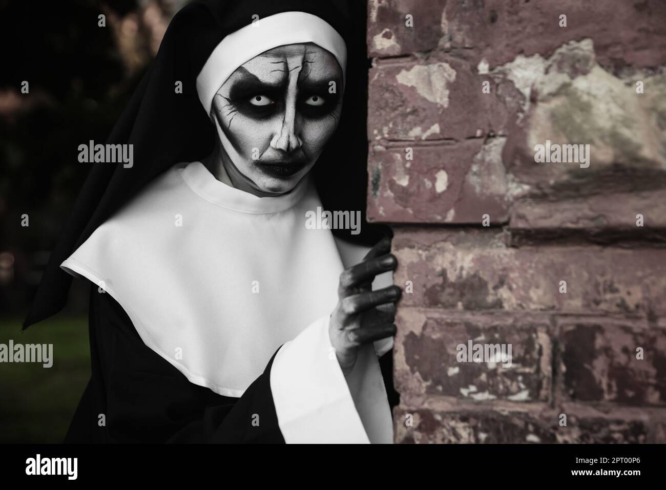 Scary devilish nun hiding behind red brick wall outdoors. Halloween ...