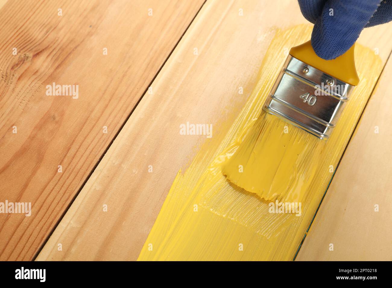 Worker applying yellow paint onto wooden surface, closeup. Space for ...