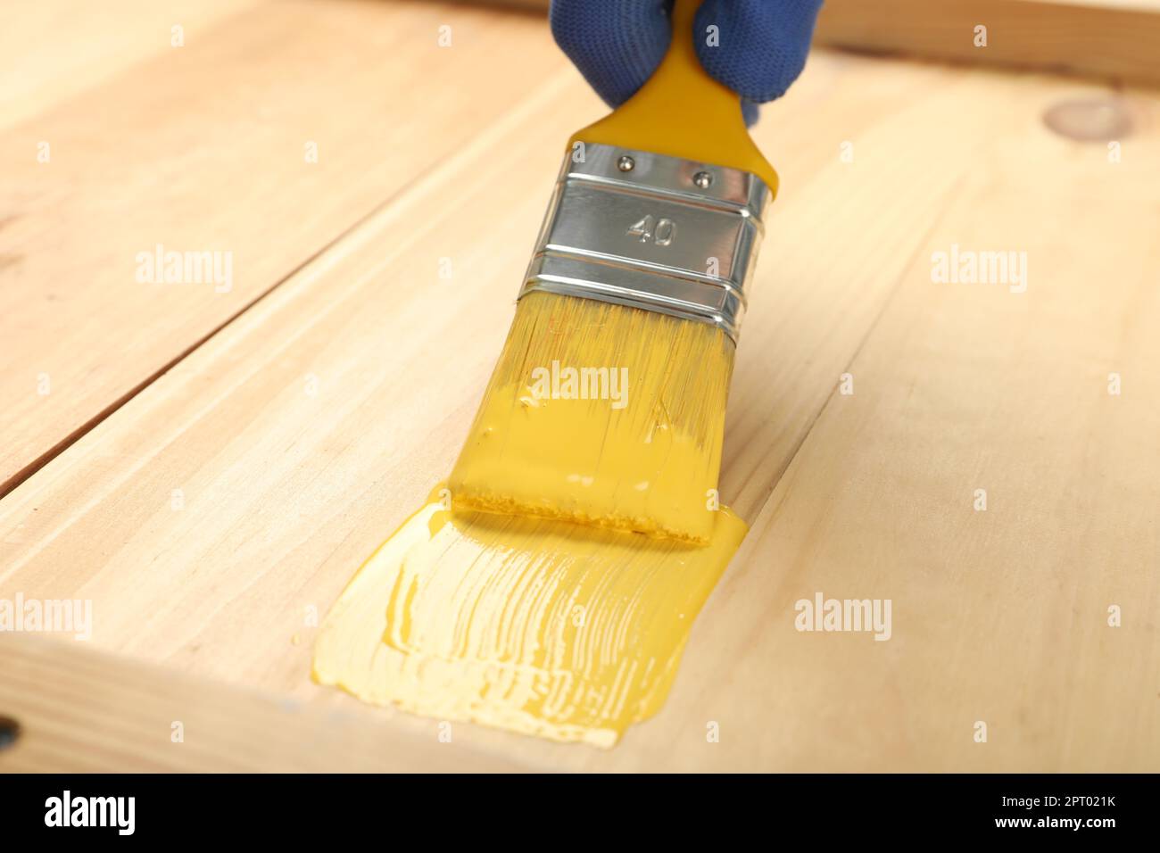 Worker applying yellow paint onto wooden surface, closeup Stock Photo ...