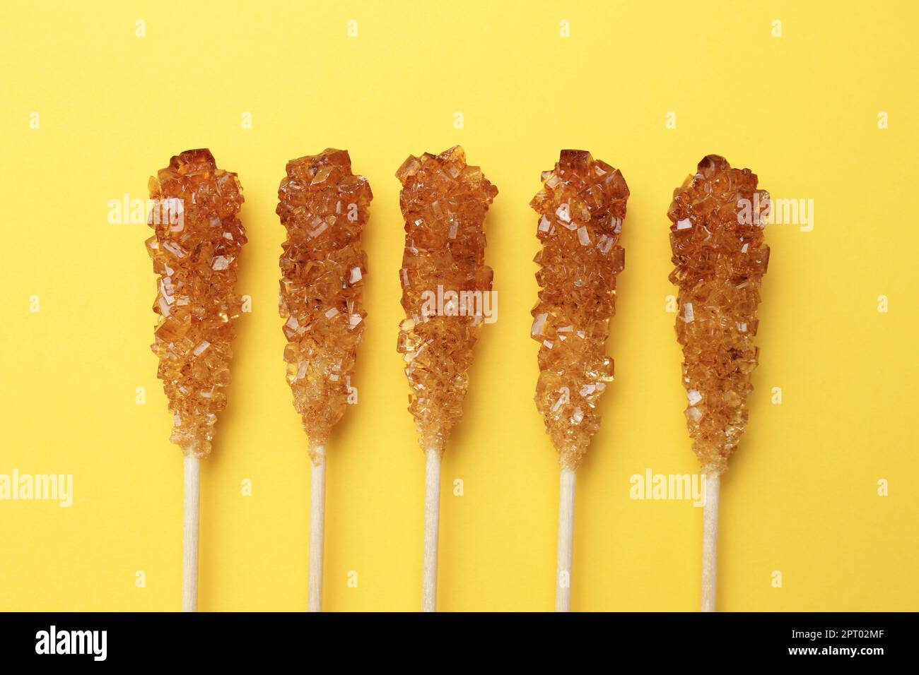 Wooden sticks with sugar crystals on yellow background, flat lay. Tasty ...