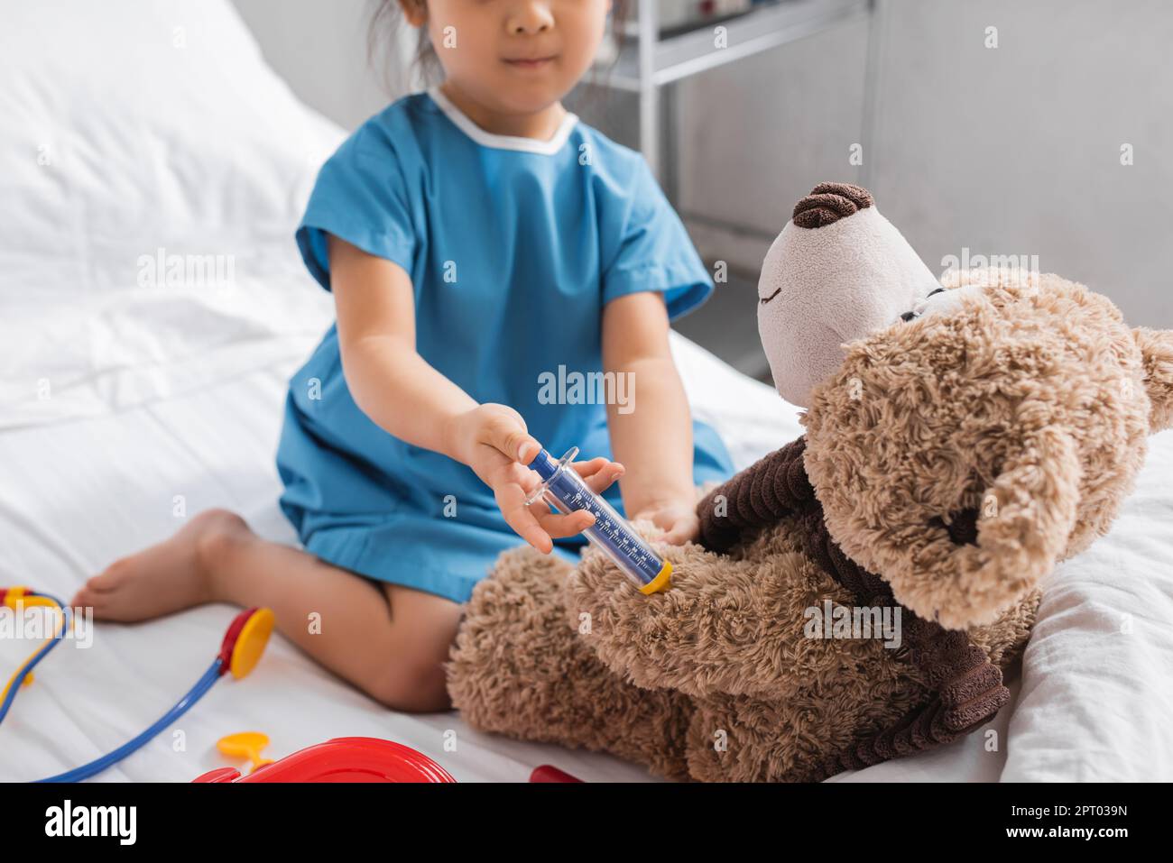 partial view of child with toy syringe doing injection to teddy bear on ...