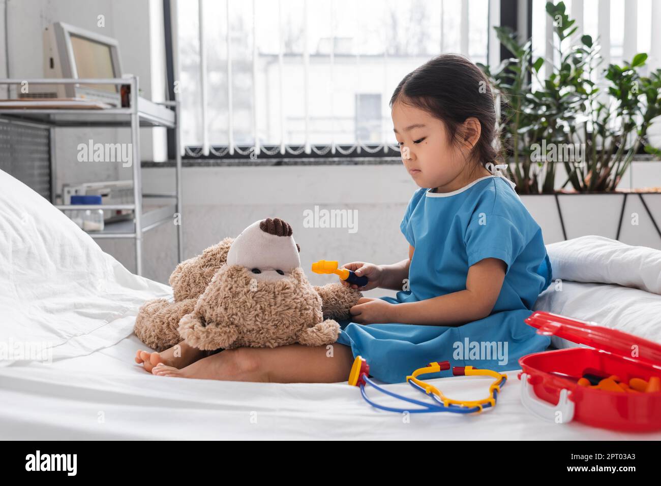 side view of little asian girl examining teddy bear with toy reflex ...