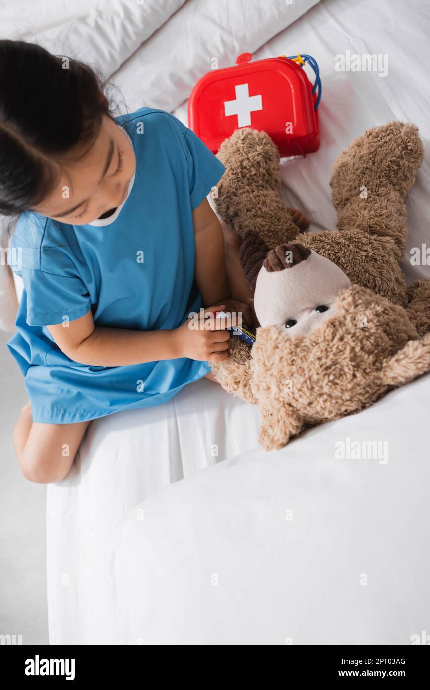 top view of asian child with toy syringe doing injection to teddy bear ...