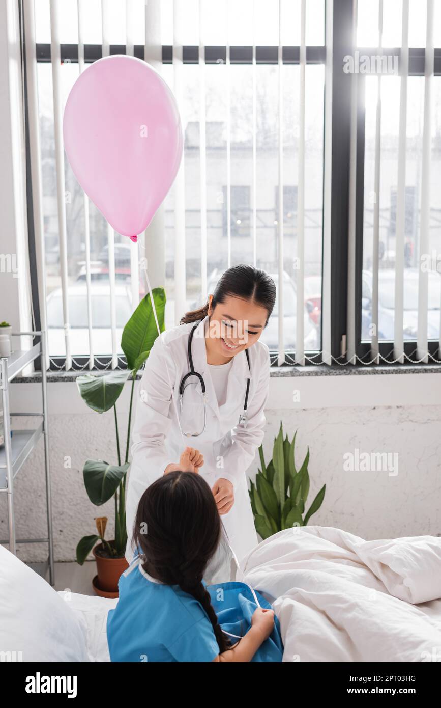 joyful asian doctor giving festive balloon to little patient in pediatric hospital,stock image ...