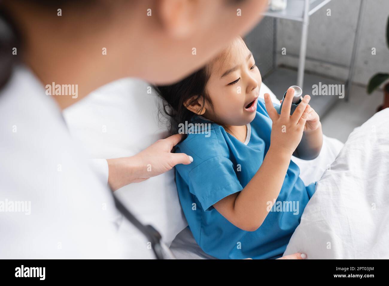 blurred pediatrician touching shoulder of asian child using inhaler in ...