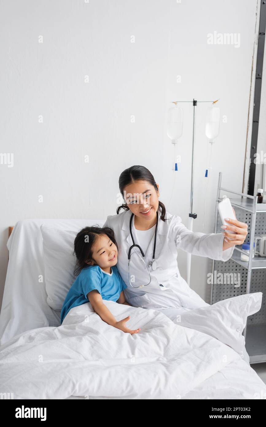happy doctor in white coat taking selfie with positive asian child in ...