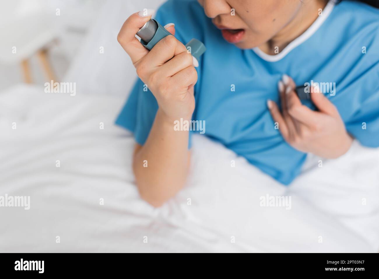 partial view of diseased woman in hospital gown using inhaler in clinic ...