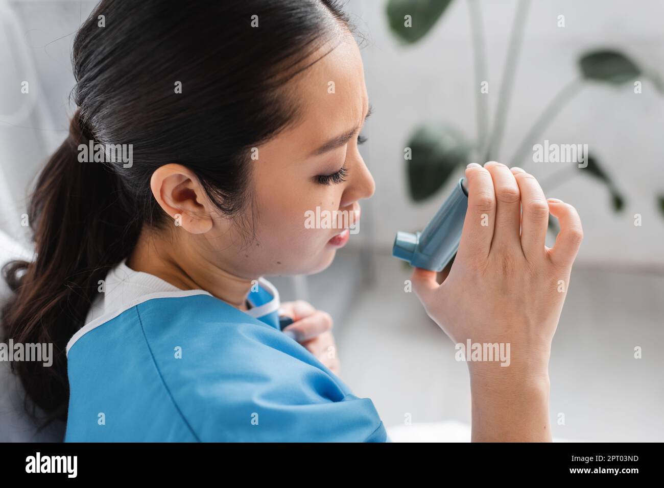 side view of diseased asian woman holding inhaler in hospital ward ...