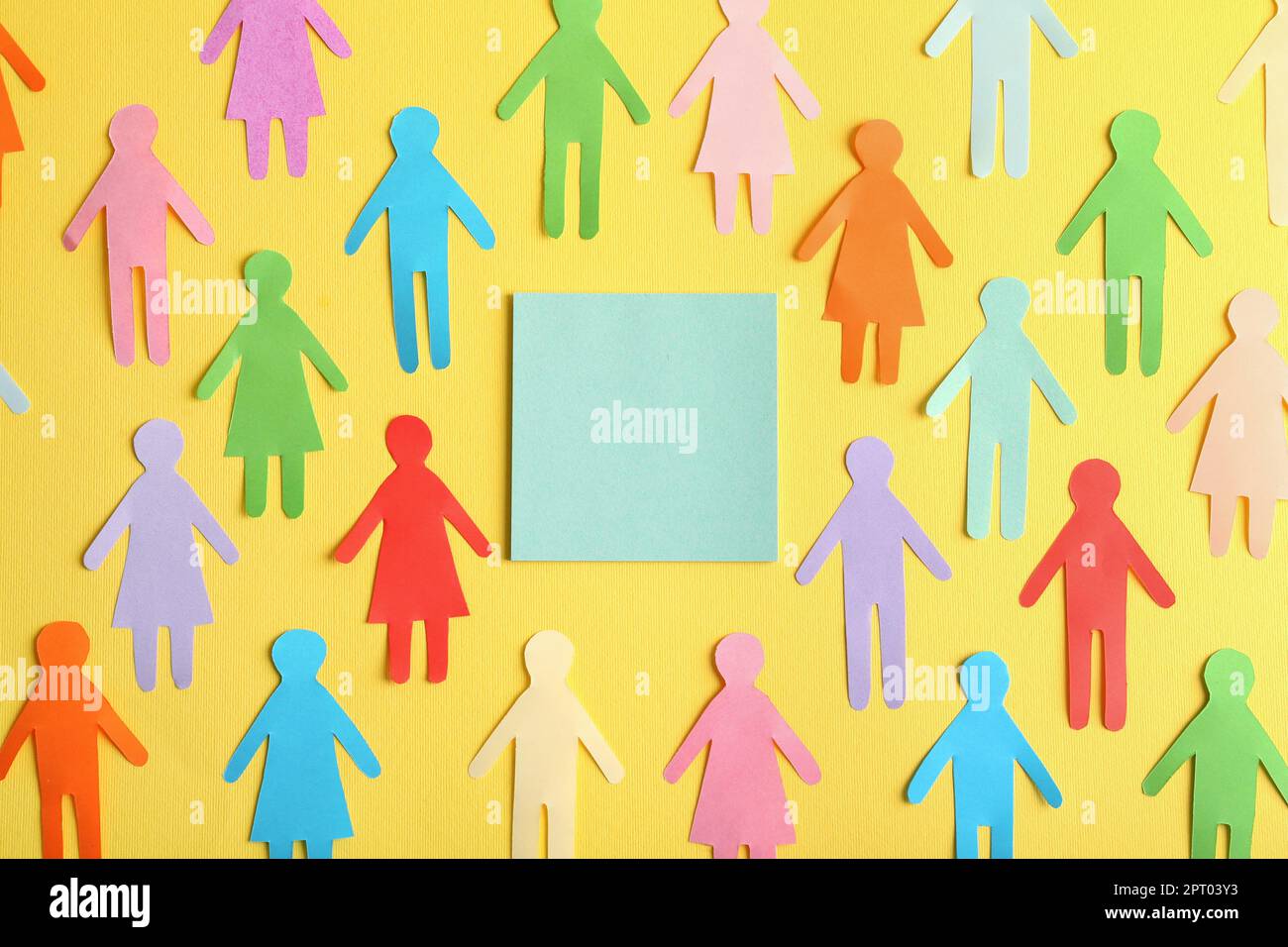 Many different paper human figures around blank card on yellow ...