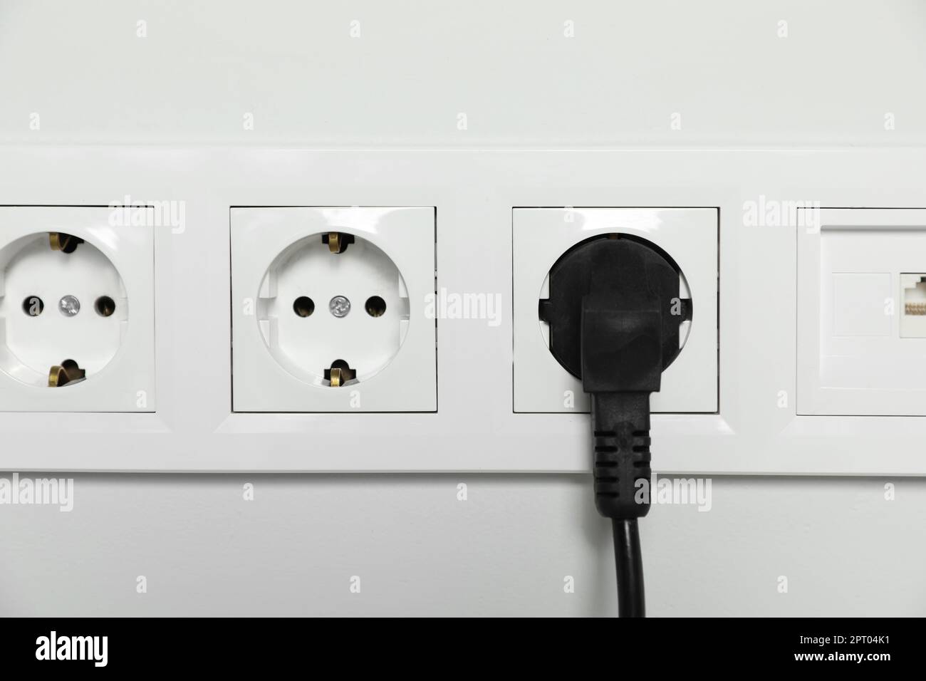 Power sockets with inserted plug on white wall, closeup. Electrical ...