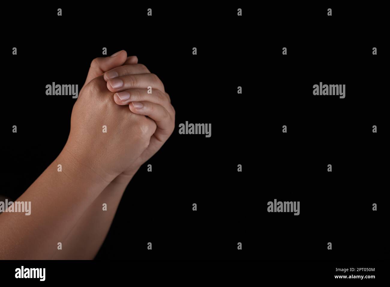 Woman holding hands clasped while praying on black background, closeup ...