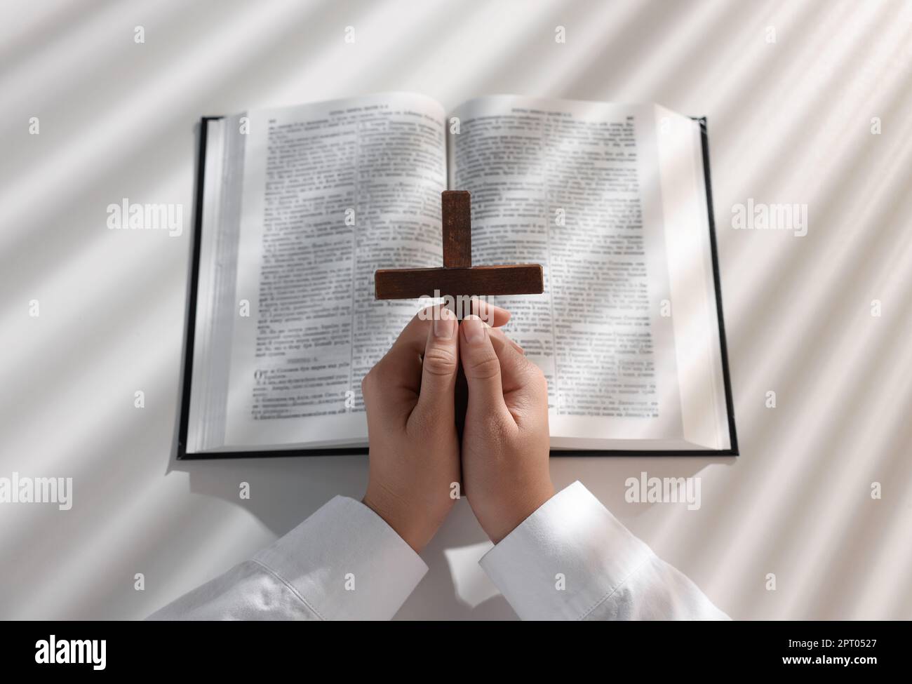 Above view of woman praying with wooden cross over Bible at white table ...