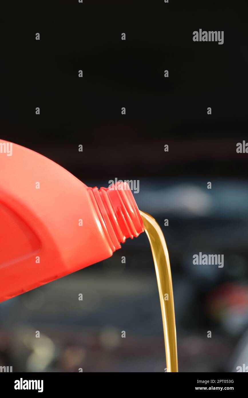Pouring motor oil from red container on blurred background, closeup ...