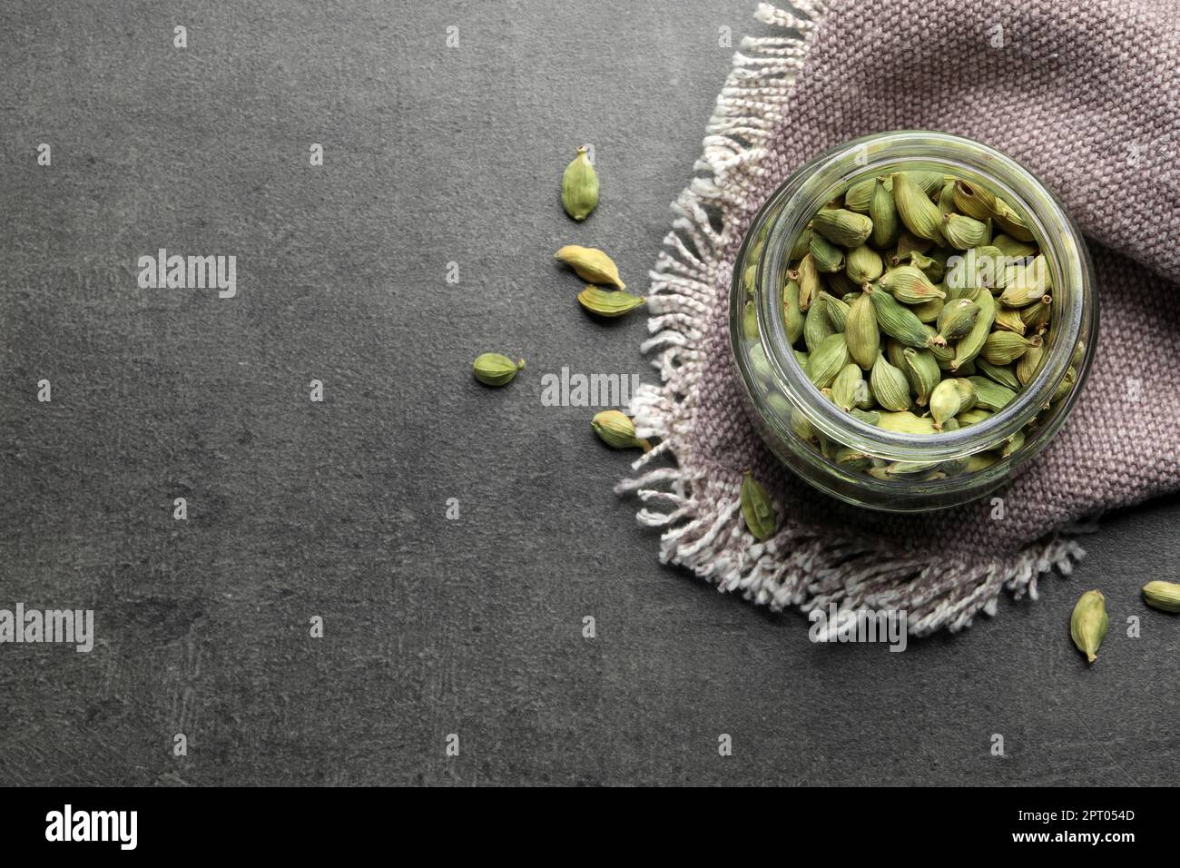 Jar with dry cardamom pods on dark grey table, flat lay. Space for text ...