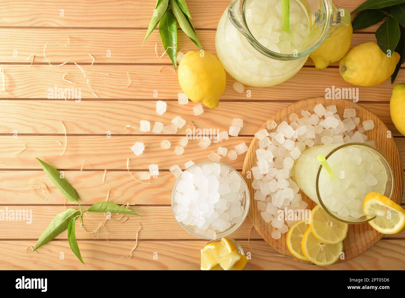 Iced lemon drink in a pitcher and glass on a wooden table with fruit ...