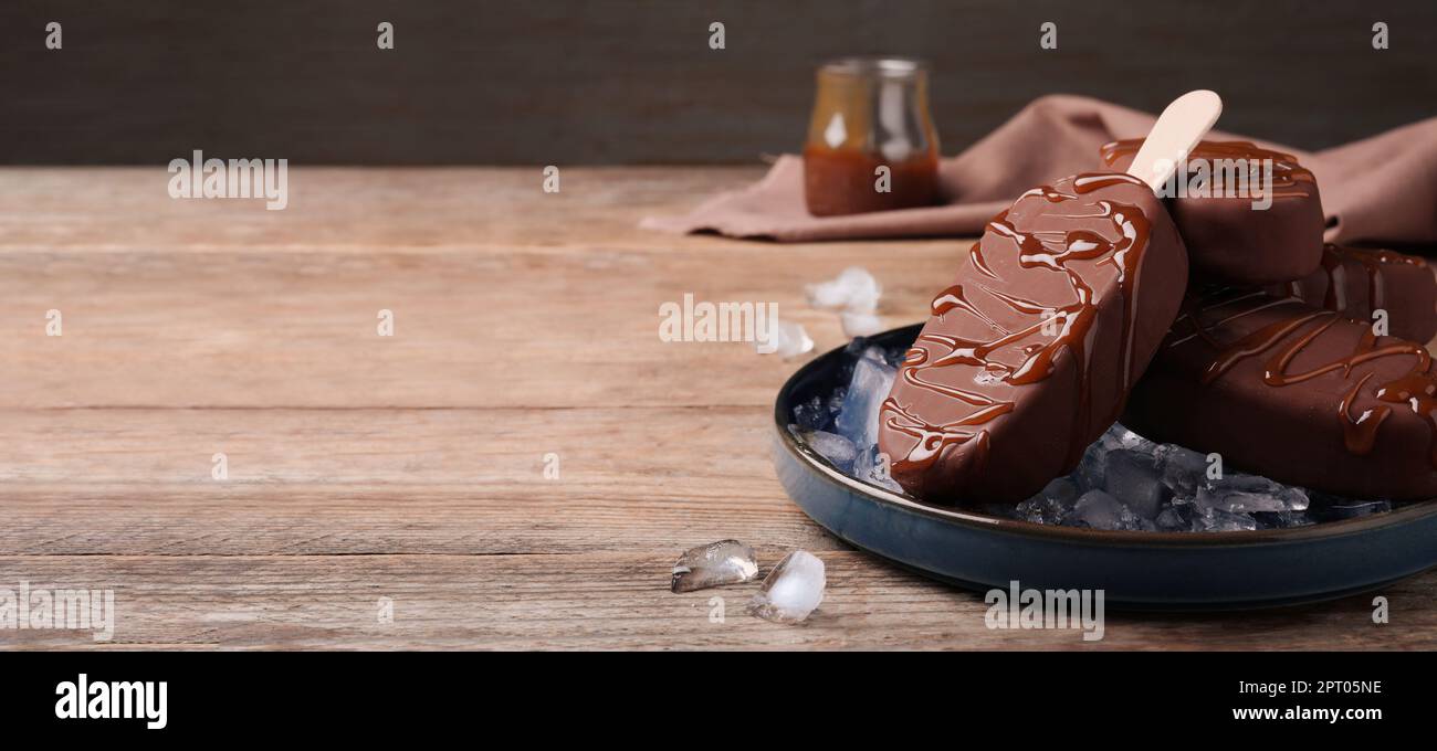 Delicious glazed ice cream bars and ice cubes on wooden table, space ...