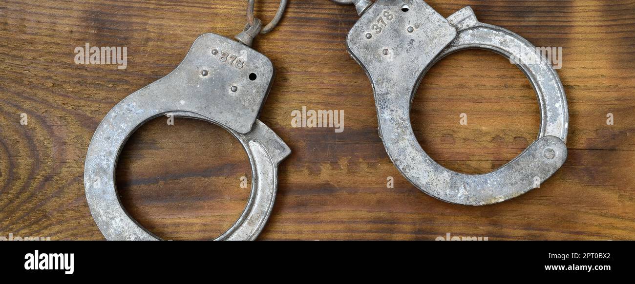 Old and rusty police handcuffs lie on a scratched wooden surface. The ...