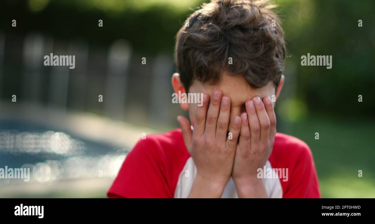 Upset child boy covering face with hand outside Stock Photo - Alamy