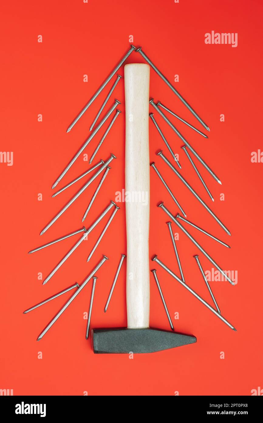 Long nails and hammer, laid out in shape of Christmas tree on red ...
