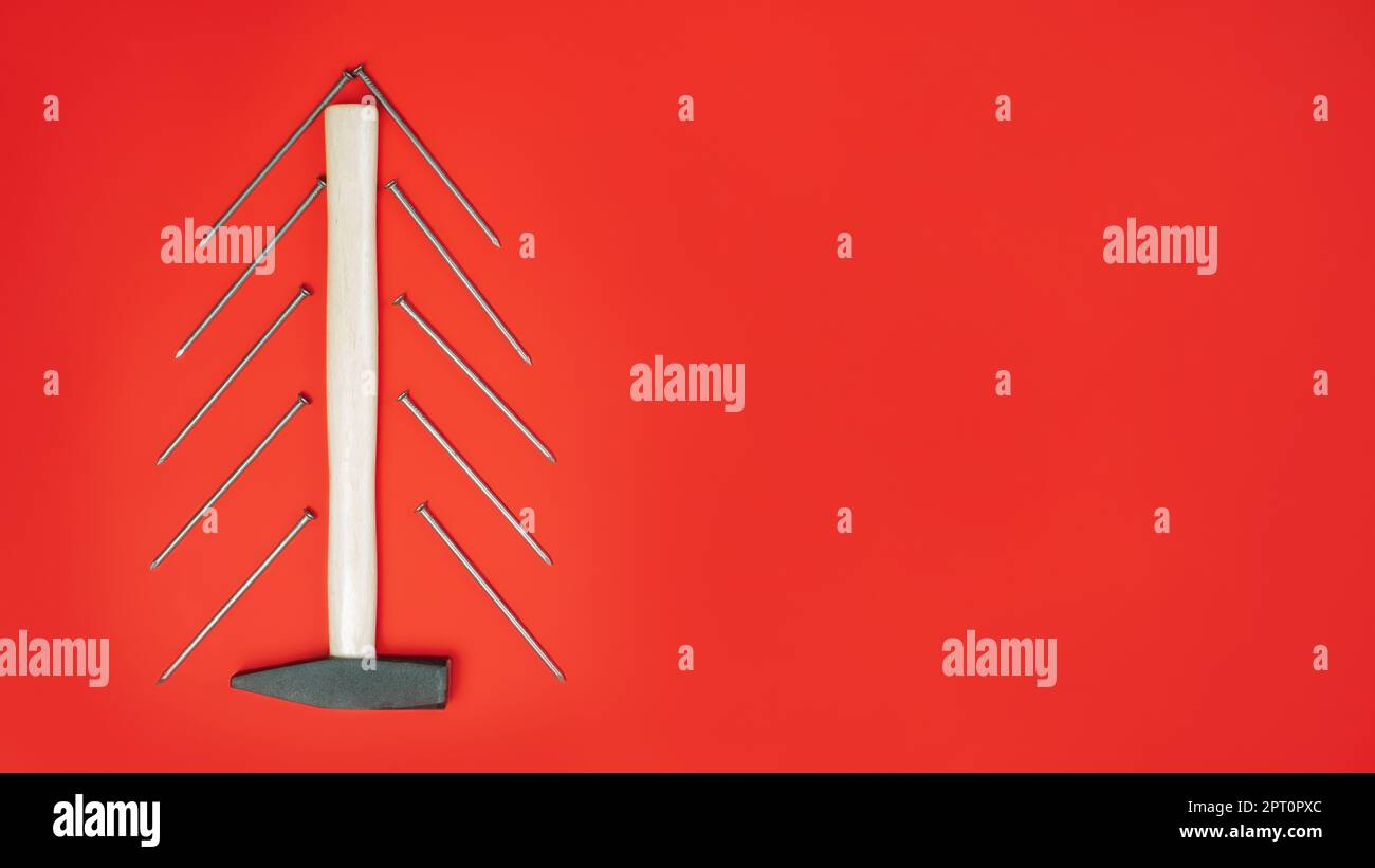 Long nails and hammer, laid out in shape of Christmas tree on red ...