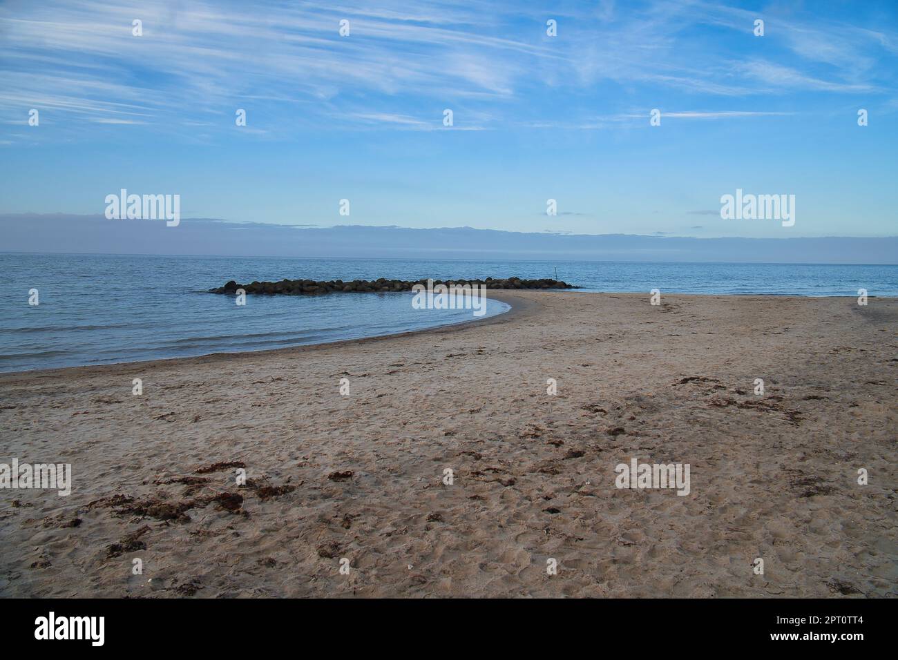 Sandy beach on the coast of Denmark. Stone groyne in the bay, sunshine ...