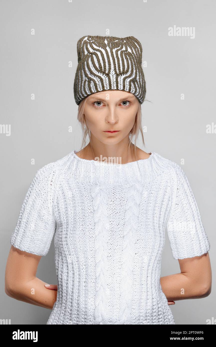 Pretty fashion model in white sweater and knitted hat hides hands ...