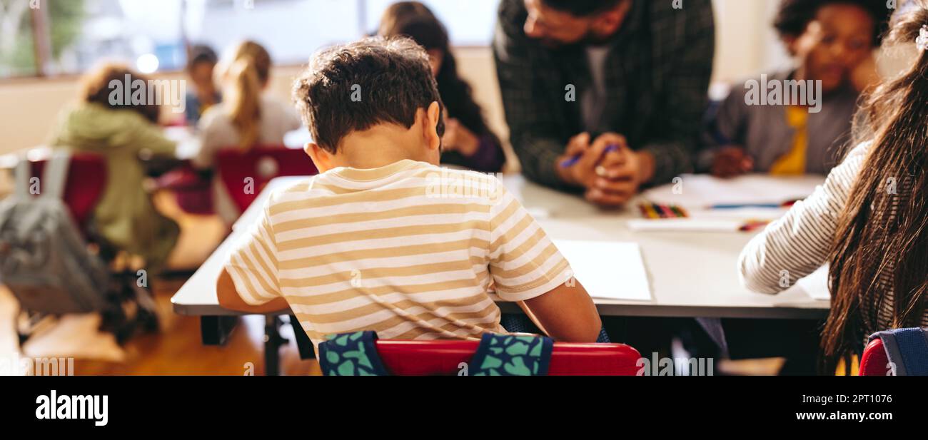 Rearview of a small boy doing his work in a primary school class. Male ...