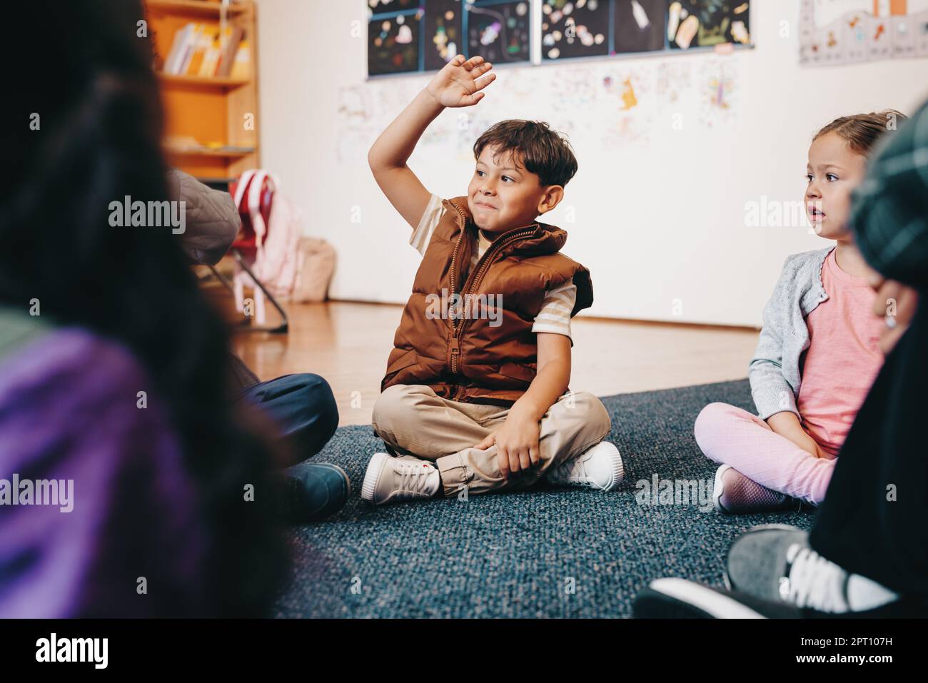Smart elementary school kid raises his hand to give an answer in class ...